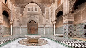 Um interior amplo com trabalhos em azulejos detalhados, uma fonte central e arcos altos.