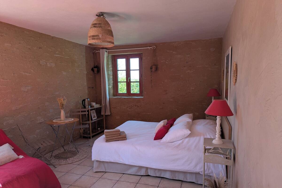 Quarto com cama, uma mesinha, uma cadeira, uma janela e luminária suspensa.