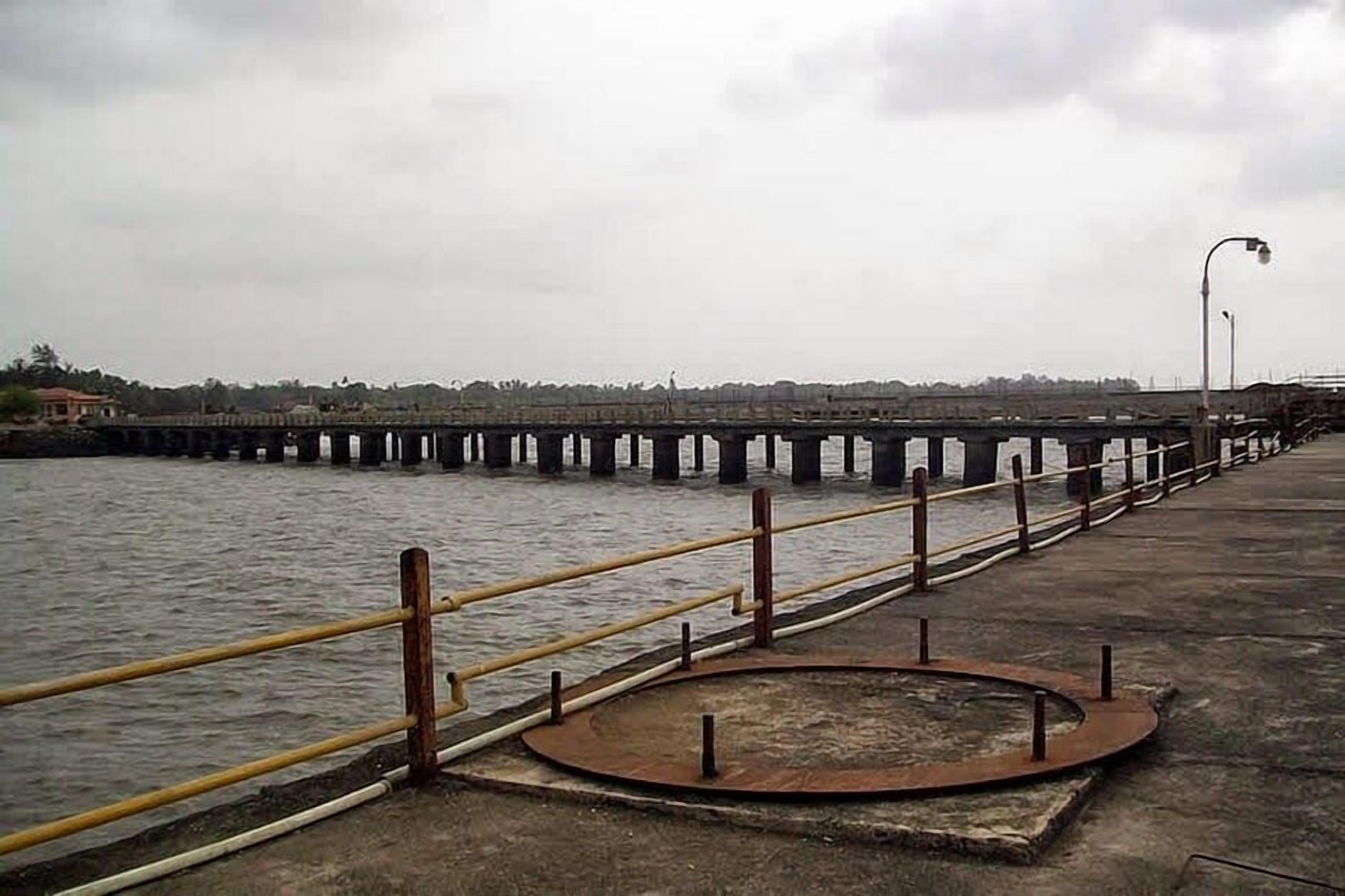 Um calçadão à beira-mar com um passeio de concreto, guarda-corpo de metal e uma plataforma circular de observação.