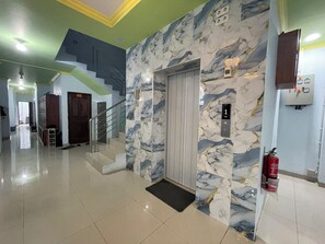 Um saguão de hotel com uma parede de mármore, uma escadaria e um extintor de incêndio.