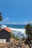 Cena costeira com um pequeno edifício, terreno rochoso e o oceano.