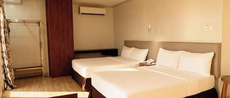 Quarto de hotel com duas camas, um banco, aparelho de ar condicionado e área de chuveiro.