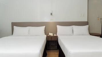 Quarto de hotel com duas camas de solteiro, uma mesa de cabeceira com telefone e um lustre.