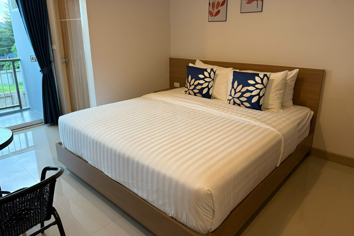 Quarto de hotel com uma cama grande, uma cadeira, uma mesa e varanda com cortinas.
