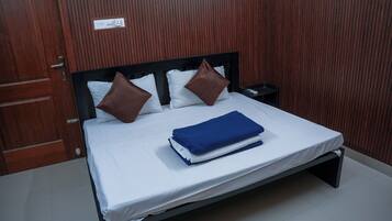 Uma cama bem arrumada com lençóis brancos e duas almofadas marrons, um cobertor azul e uma mesa de cabeceira com um telefone.