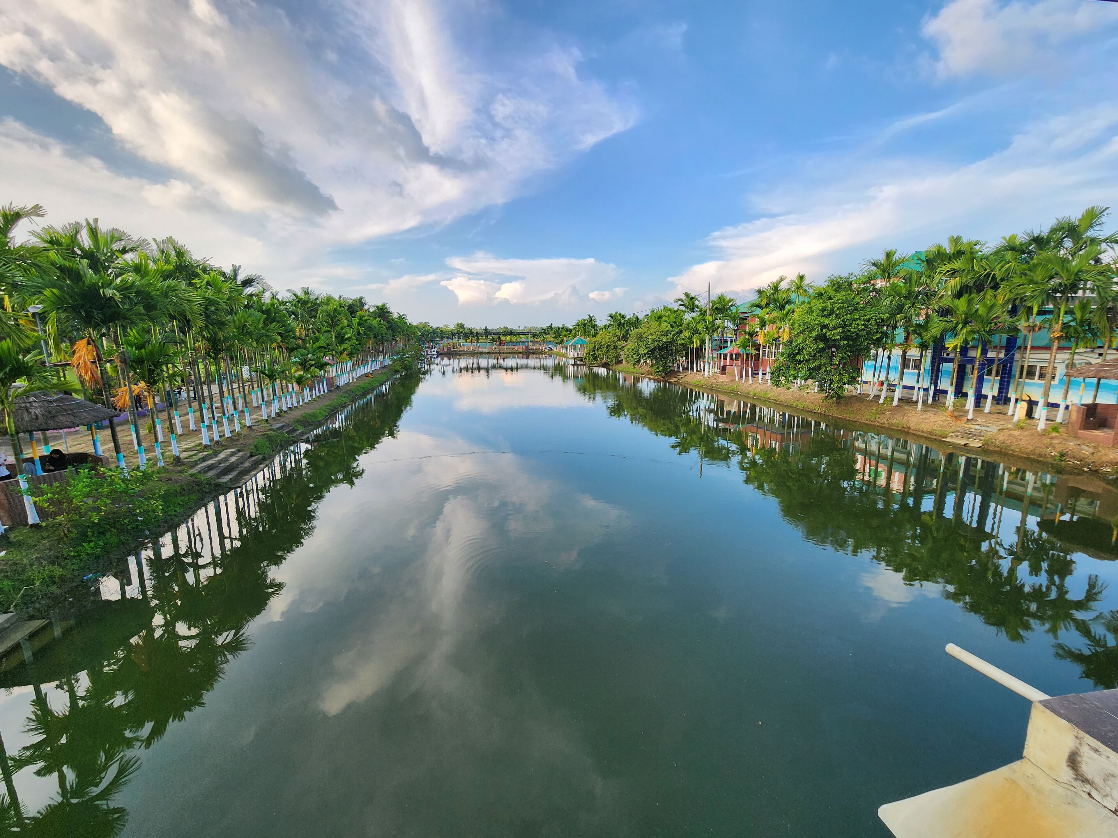 Um rio calmo com reflexo nítido do céu e vegetação ao redor.