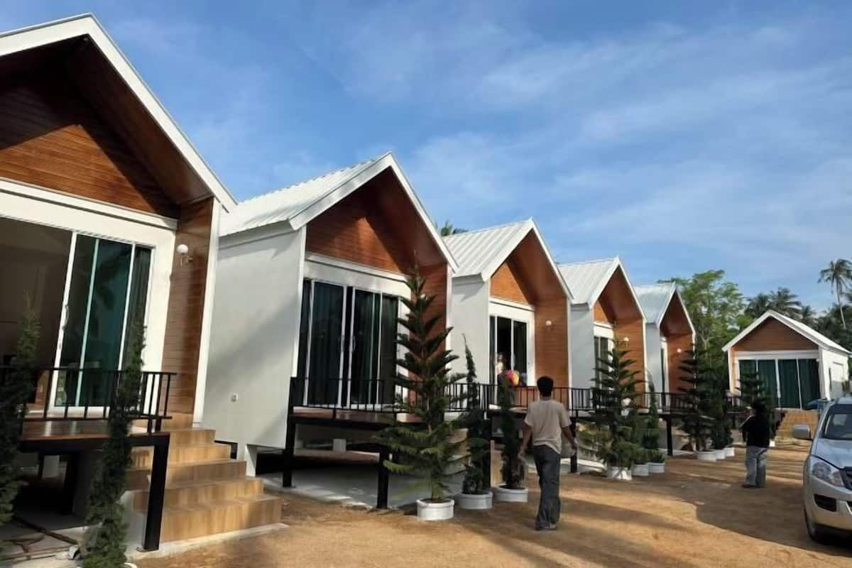 Fileira de cabanas modernas com telhados de madeira e grandes janelas, além de um caminho de acesso pavimentado.