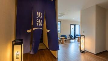 Corredor de hotel com piso de madeira, cortina azul com caracteres japoneses e um tradicional lampião japonês.