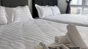 Quarto de hotel com duas camas, roupa de cama branca, um copo de água e uma toalha enrolada sobre uma das camas.
