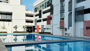 Um edifício moderno com piscina central, várias varandas e céu claro.
