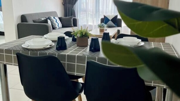 Uma área de refeições com mesa posta para quatro pessoas, um sofá e uma luminária.