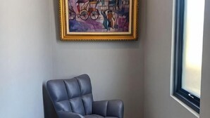 Quarto de canto com poltrona de couro cinza, uma pintura abstrata emoldurada e uma janela.