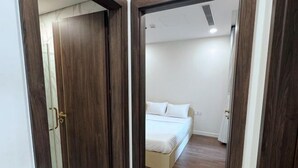Quarto com cama, piso de madeira e parede branca.