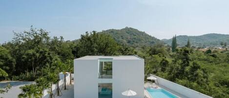 Um edifício moderno com piscina, cercado por vegetação e colinas.