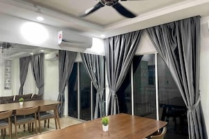 Quarto com mesa de jantar, cadeiras, ventoinha no teto e uma janela grande com cortinas.