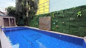 Piscina com chão em azulejos, cercada por uma parede verde com plantas e um elemento decorativo em pedra.