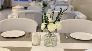 Mesa de jantar posta com pratos brancos, um copo transparente e um vaso com flores brancas.