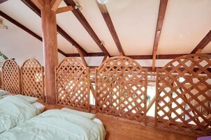 Quarto com estrutura de cama em madeira, divisória de ripas e teto com vigas de madeira.