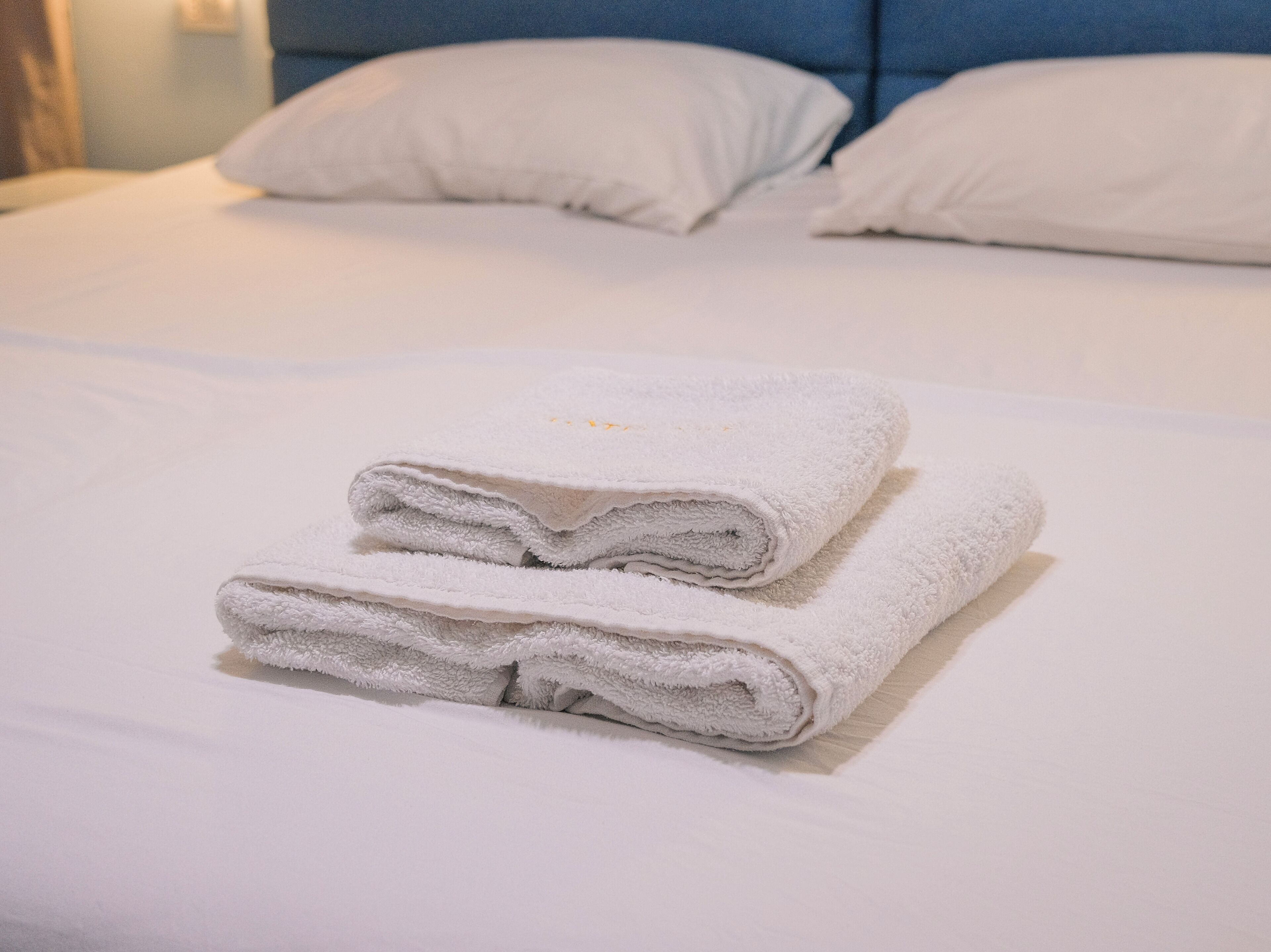 Cama bem arrumada com duas toalhas brancas dobradas e dois travesseiros brancos.