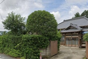 Uma casa japonesa tradicional com telhado de telhas, portão de madeira e uma grande árvore na frente.