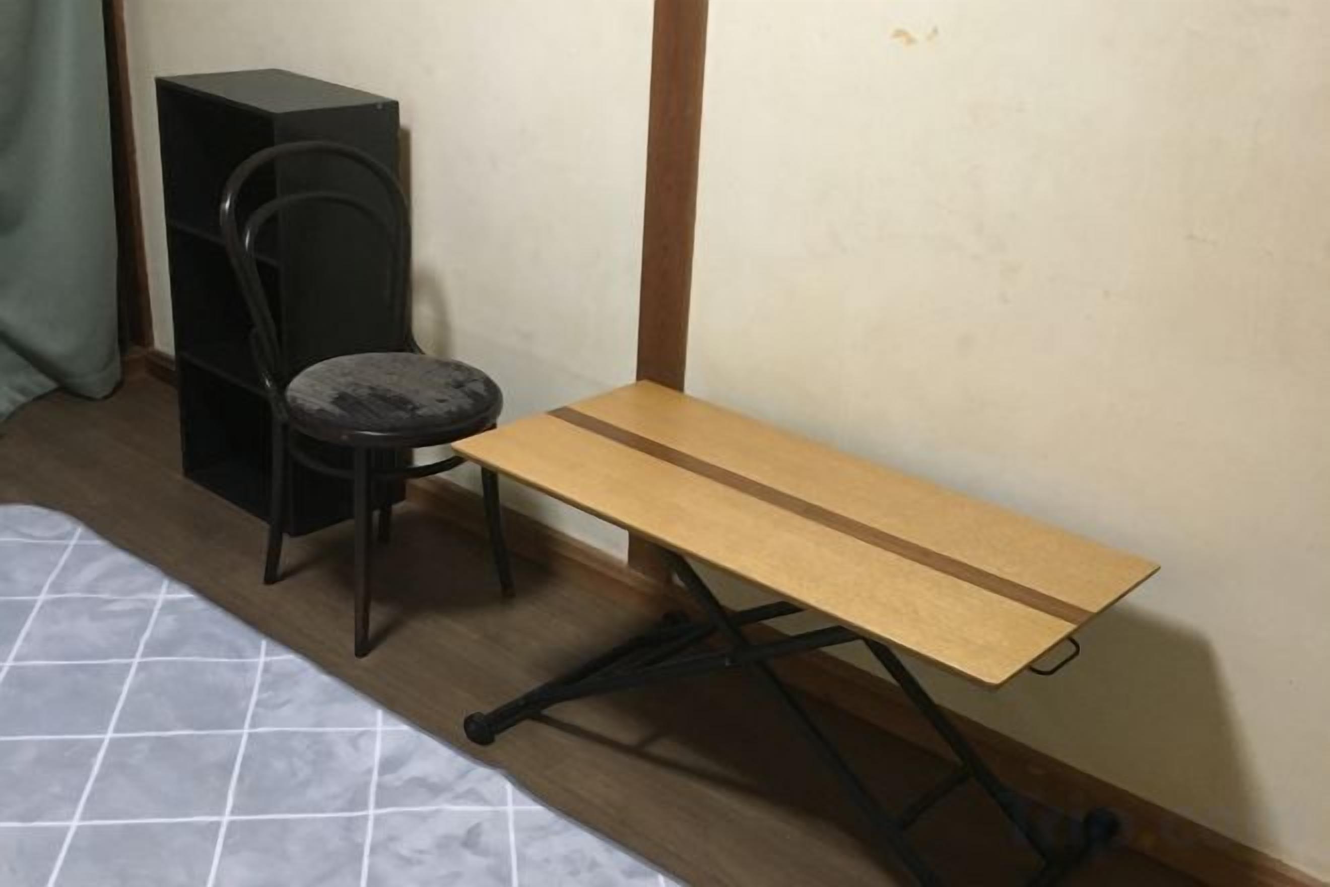 Um quarto pequeno com uma mesa de madeira, uma cadeira preta e uma estante.