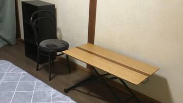 Um quarto pequeno com uma mesa de madeira, uma cadeira preta e uma estante.