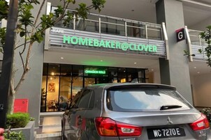 Fachada de loja com um letreiro que diz 'HOMEBAKER@CLOVER' e um carro estacionado na frente.