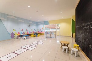 Espaço infantil com lousa, mesas, cadeiras e um jogo de amarelinha.