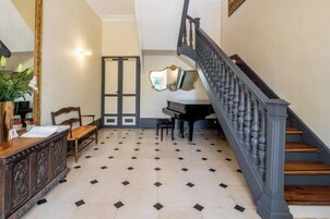 Uma imponente escadaria com guarda-corpo escuro que leva a um piano e um espelho na parede.