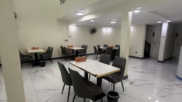 Uma sala de jantar de hotel com mesas, cadeiras, um cesto de lixo e um ventilador de teto.