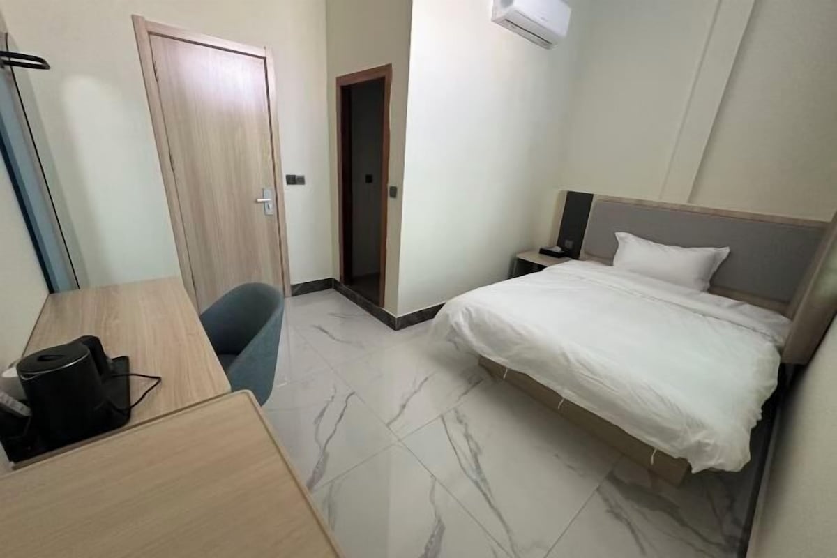 Quarto de hotel com cama, secretária, cadeira, guarda-roupa e ar condicionado.