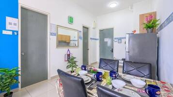 Uma sala de jantar com mesa posta para quatro, cadeiras, geladeira e espelho na parede.