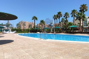 Piscina com deck revestido, cercada por palmeiras e céu claro.