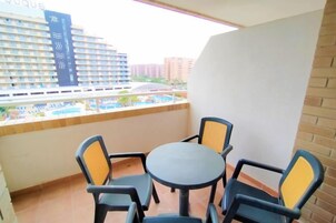 Varanda com mesa e cadeiras, vista para uma piscina e edifícios.