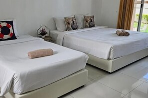 Quarto de hotel com duas camas, roupa de cama branca, uma mesa de cabeceira e uma janela com cortinas.