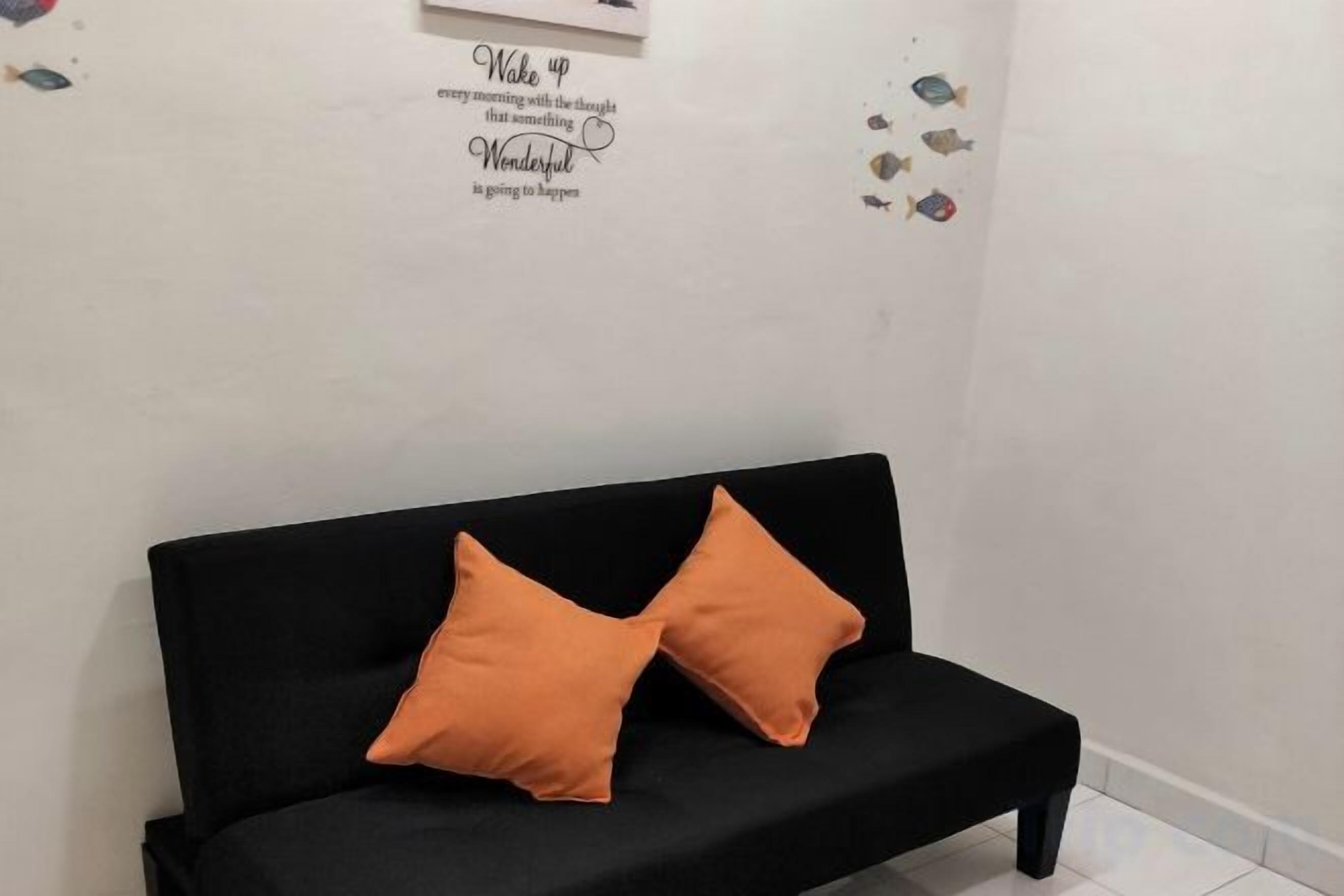 Sofá preto com duas almofadas laranja em frente a uma parede com frase motivacional e pequenos adesivos de peixes.