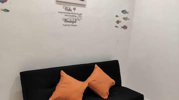 Sofá preto com duas almofadas laranja em frente a uma parede com frase motivacional e pequenos adesivos de peixes.