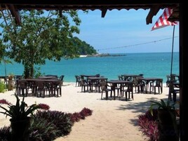 Espaço de estar ao ar livre com mesas e cadeiras voltado para uma praia, sob uma estrutura coberta com uma bandeira americana.