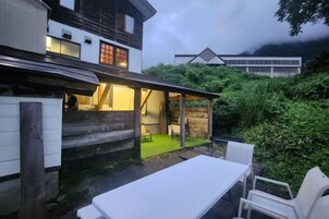 Uma casa japonesa tradicional com fachada de madeira, área de estar coberta ao ar livre e um pequeno jardim.
