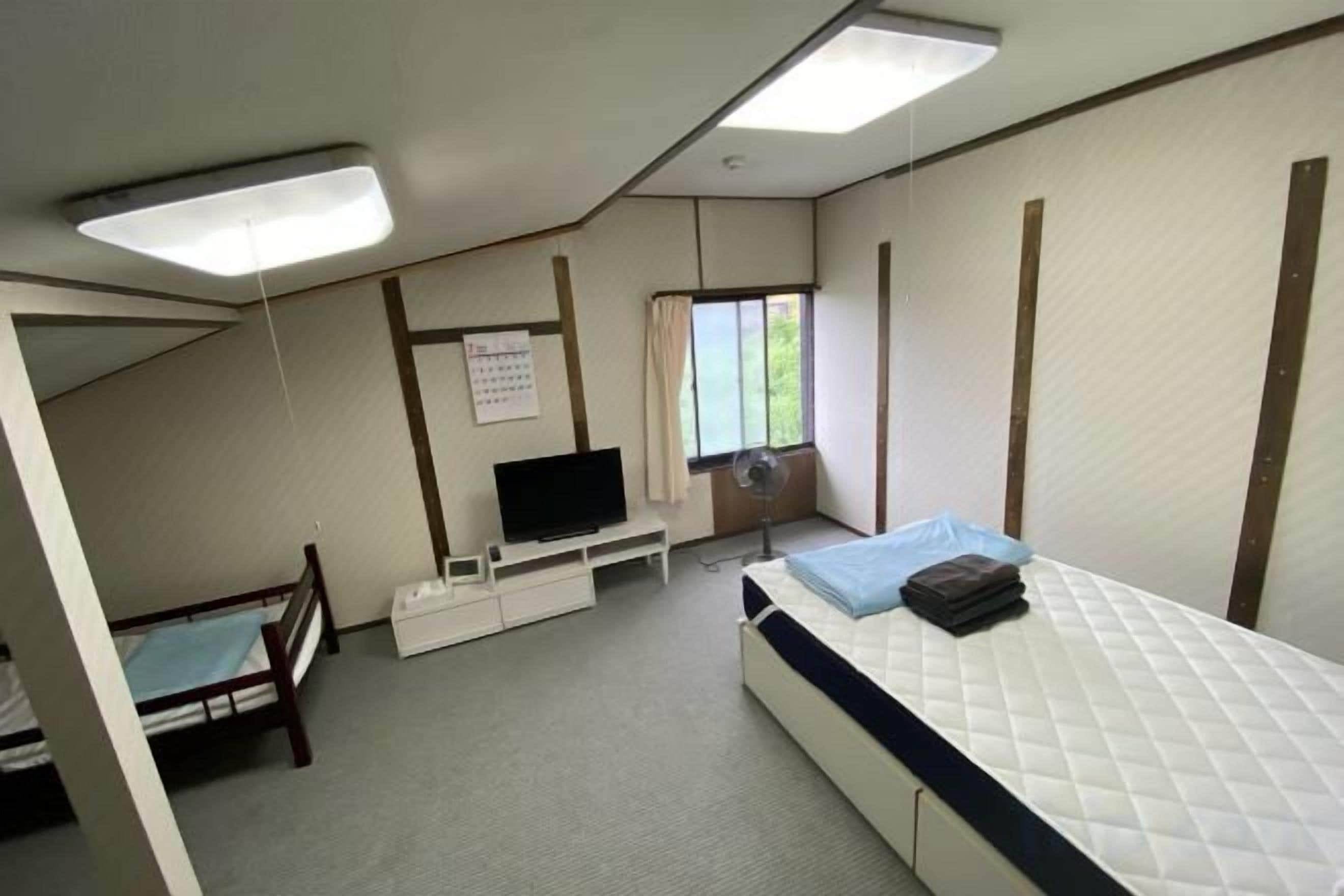 Quarto compacto com cama, televisão, escrivaninha e janela.