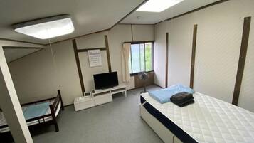 Quarto compacto com cama, televisão, escrivaninha e janela.