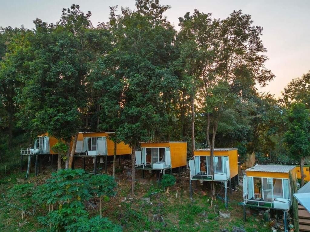 Uma fileira de cabanas em estilo de casa na árvore, com plataformas elevadas, rodeadas por uma floresta densa.