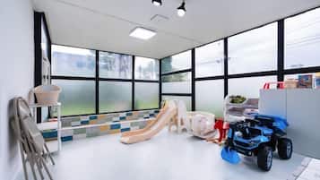 Um quarto espaçoso com grandes janelas, um escorrega, área de recreação e um carrinho de brinquedo.