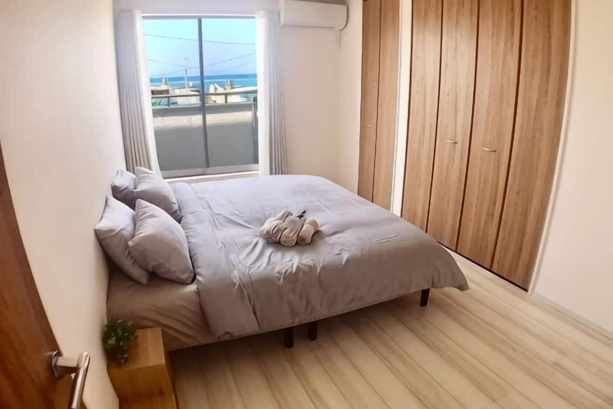Quarto com cama, janela, guarda-roupa de madeira e uma pequena planta.