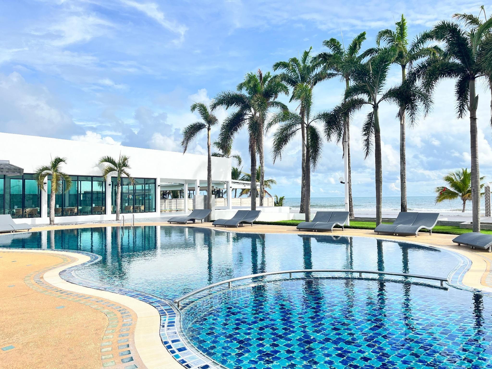 Uma área de piscina com espreguiçadeiras, palmeiras e vista para o oceano.
