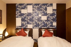 Quarto de hotel com duas camas, parede estampada e mesa de cabeceira com abajur.