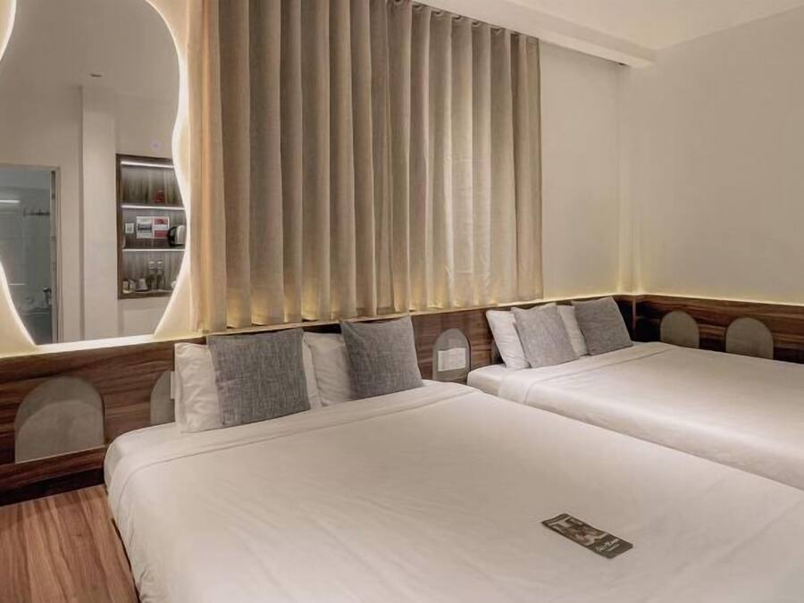 Quarto de hotel com duas camas, cabeceira de madeira, um espelho grande e vista para o banheiro.
