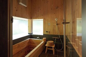 Uma cabana de madeira com uma grande banheira de madeira, um pequeno banquinho de madeira e um box de chuveiro em vidro.
