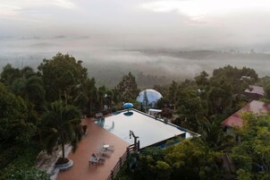Um resort com piscina, espreguiçadeiras e vista para a floresta e névoa ao redor.