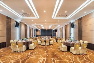 Sala de conferência com mesas redondas, cadeiras e uma tela grande.